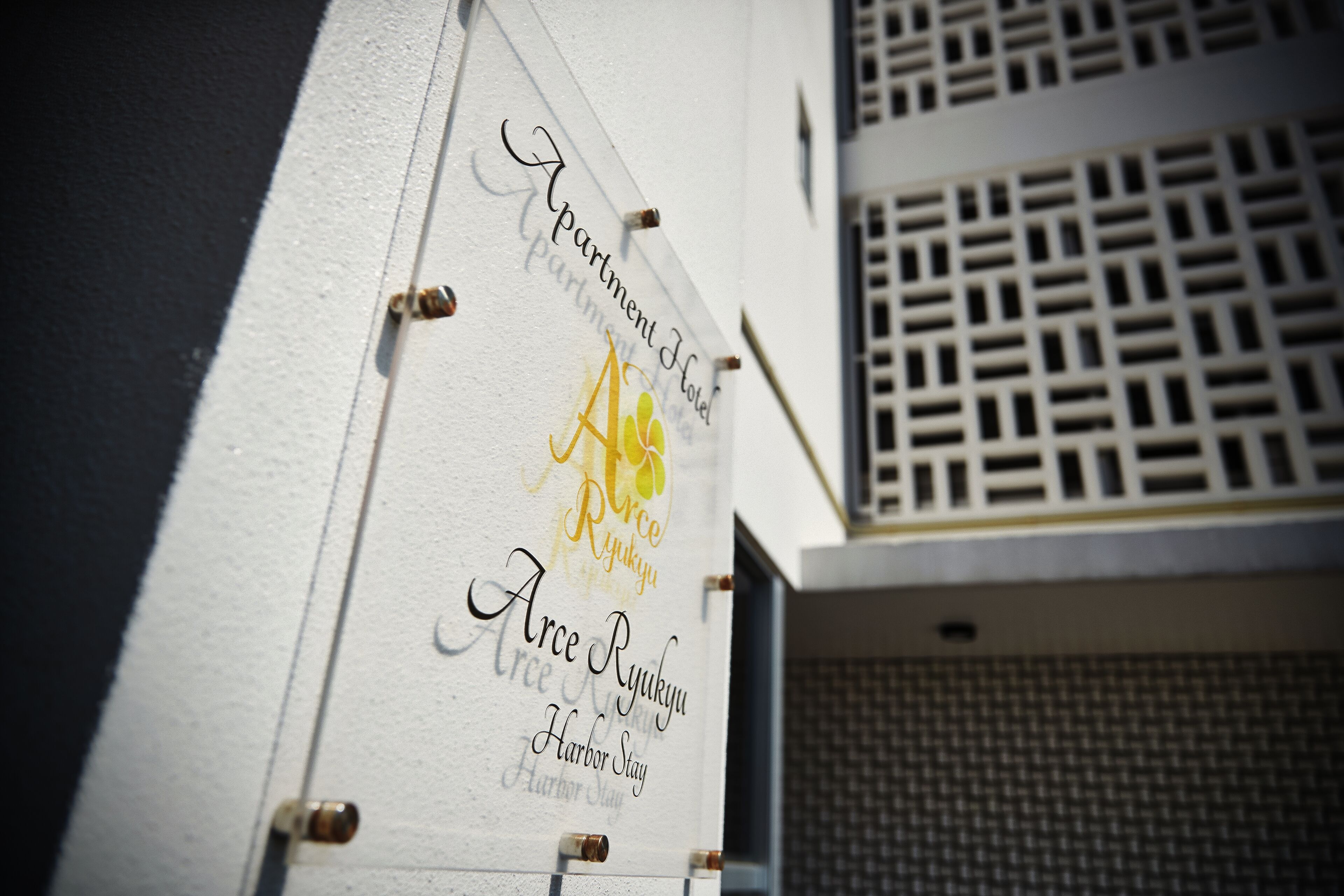Placa com a inscrição 'Apartment Hotel' e o logotipo e nome 'Arce Ryukyu Harbor Stay'.