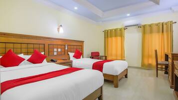 Quarto de hotel com duas camas, travesseiros vermelhos, cabeceira de madeira, uma escrivaninha, uma cadeira e um aparelho de ar condicionado.