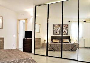 Quarto com um espelho grande, cama com roupa de cama estampada, cômoda e obras de arte na parede.