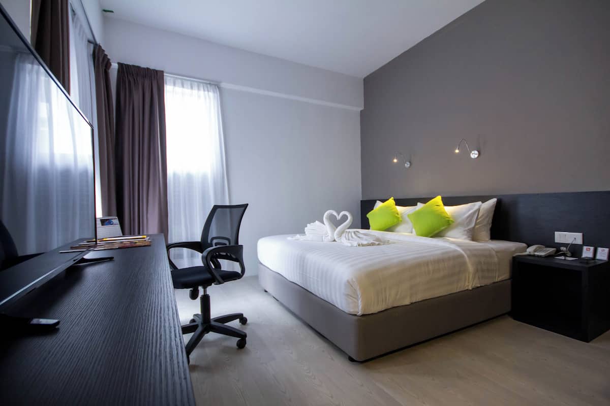 Quarto de hotel com cama, escrivaninha, cadeira e mesa de cabeceira.