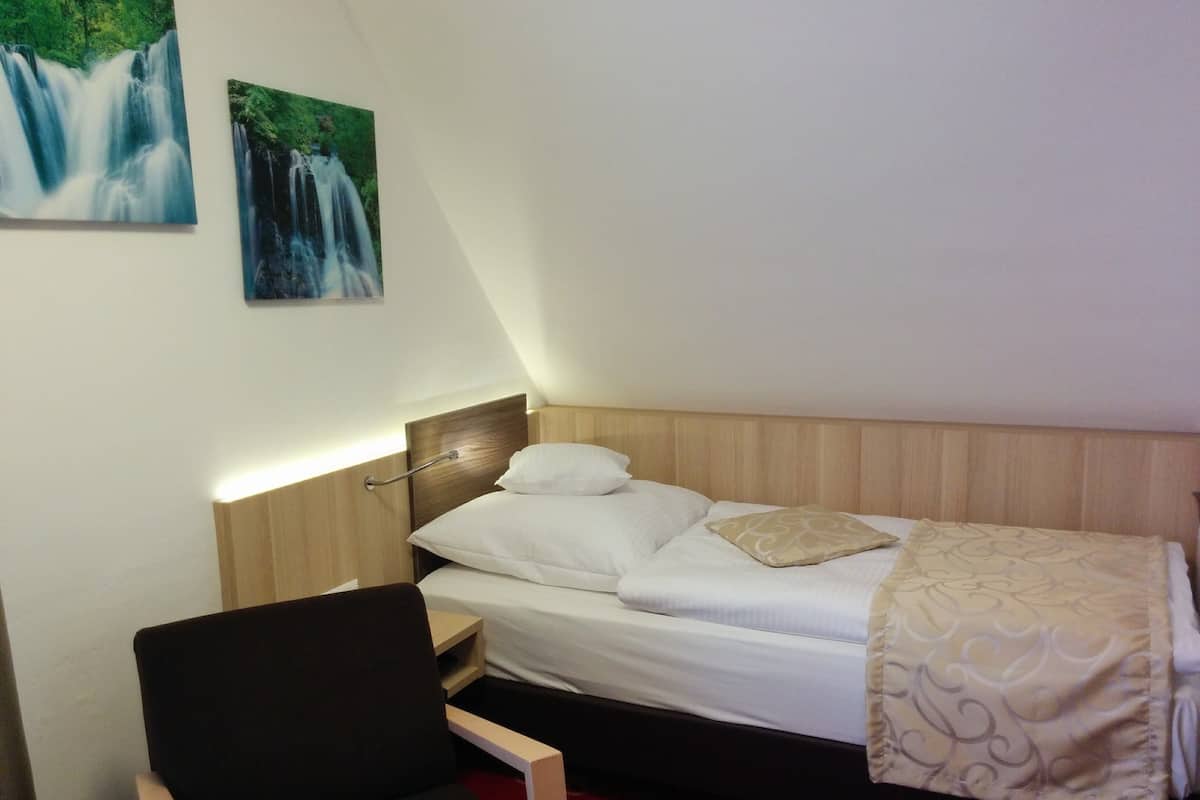 Quarto de hotel com uma cama, uma cadeira e duas imagens de cachoeiras fixadas na parede.