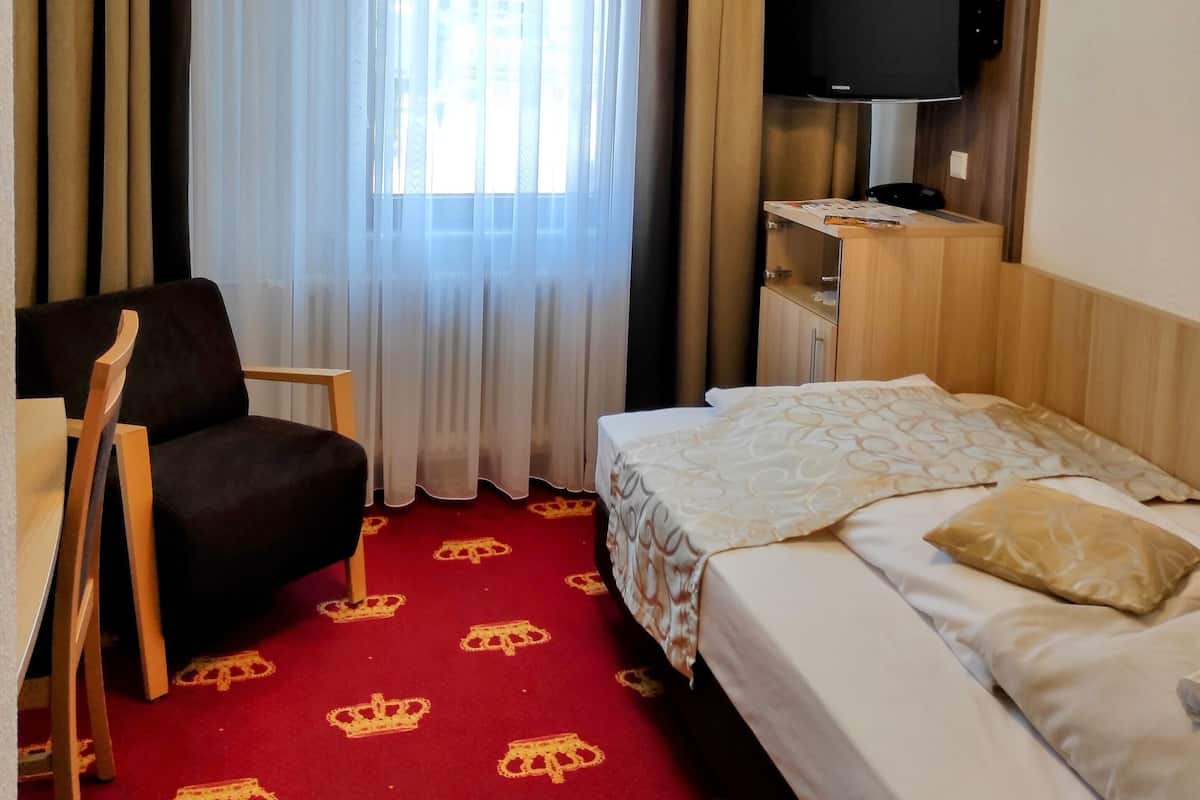 Quarto de hotel com uma cama, uma cadeira, televisão presa à parede e uma janela com cortinas.
