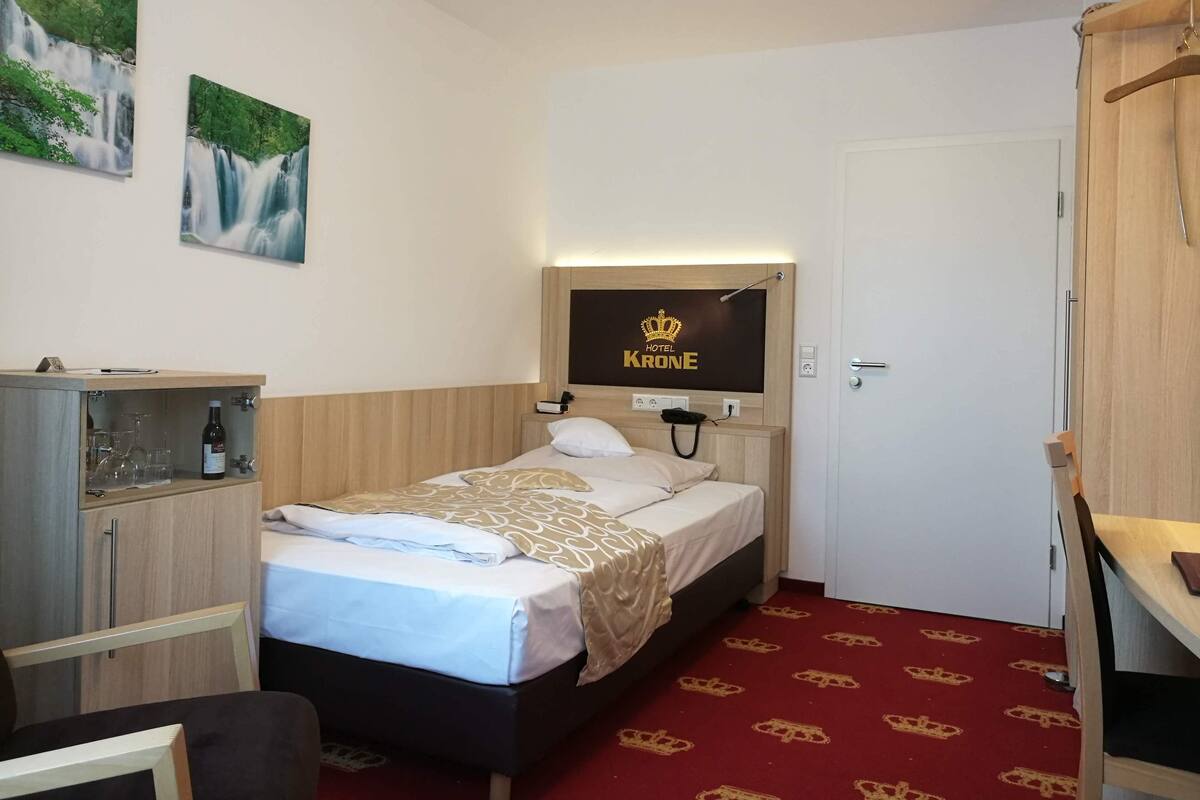 Quarto de hotel com uma cama, uma escrivaninha, um guarda-roupa e duas pinturas nas paredes.