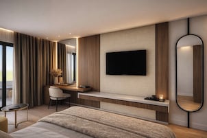 Quarto de hotel moderno com uma cama grande, uma escrivaninha com cadeira, uma TV de tela plana na parede e um espelho amplo.