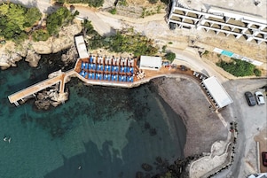 Vista aérea de um hotel à beira-mar, com um píer, área de piscina e praia.