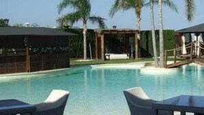 Uma área de piscina com espreguiçadeiras, palmeiras e um espaço coberto para sentar.