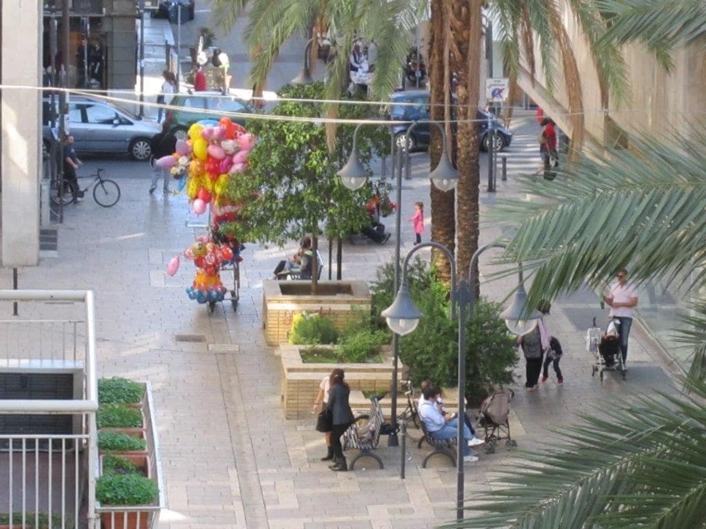 Praça pública com bancos, uma fonte e pessoas caminhando.