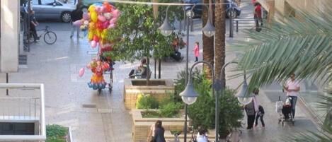 Praça pública com bancos, uma fonte e pessoas caminhando.
