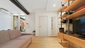 Uma sala de estar moderna com um sofá bege, piso de madeira, uma TV sobre um suporte de madeira e uma porta branca.