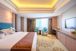 Quarto de hotel com uma cama grande, uma escrivaninha, uma televisão e vista para o exterior pela janela.