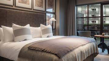 Quarto de hotel moderno com uma cama grande, vista da cidade através de janelas do chão ao teto e obras de arte emolduradas na parede.