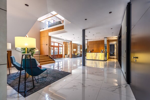 Um hall de hotel moderno com espaço amplo, balcão de recepção e escada que leva a um andar superior.