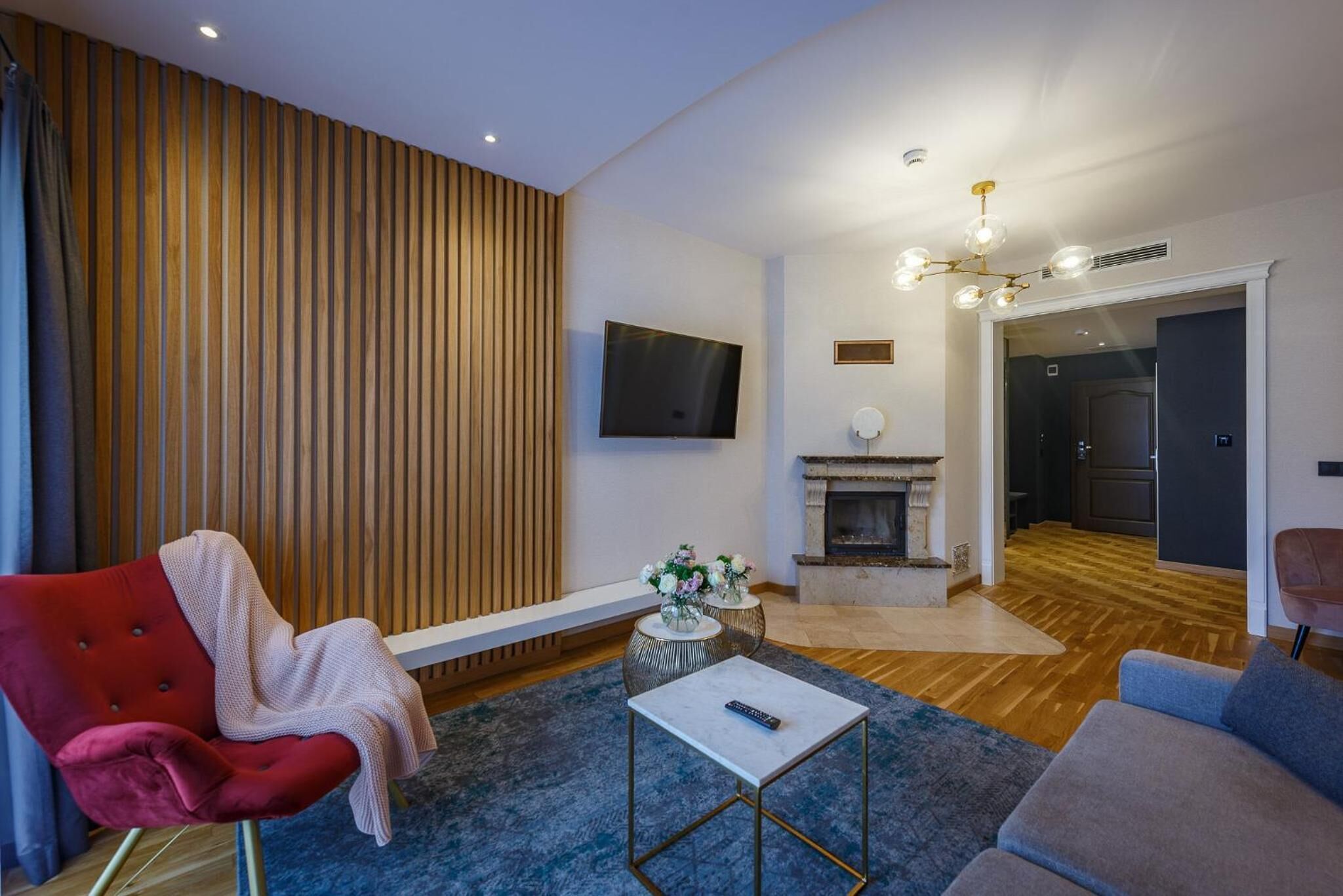 Uma sala de estar moderna com uma poltrona vermelha, um sofá, uma lareira e uma televisão na parede.