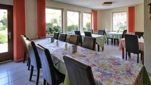Uma sala de jantar com uma mesa comprida, cadeiras e grandes janelas.