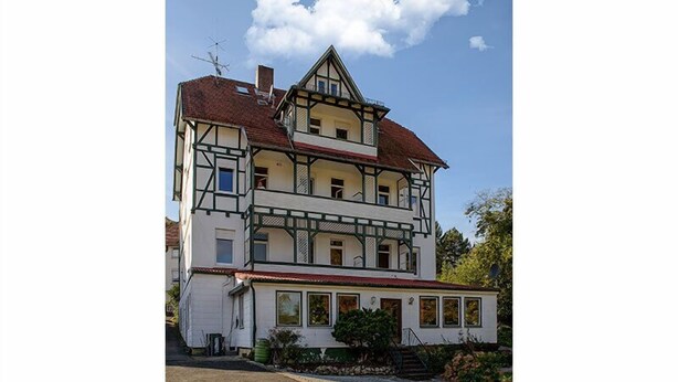 Um edifício de vários andares com estilo arquitetônico tradicional, destacando-se uma varanda saliente no segundo pavimento.