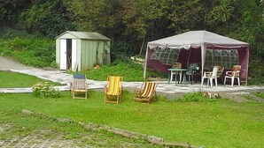 Um pequeno abrigo e uma tenda com cadeiras e uma mesa, cercados por vegetação.