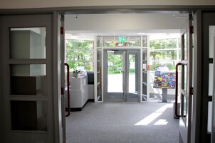 Uma área de recepção com porta de vidro, balcão de recepção e um mural com diversos avisos.