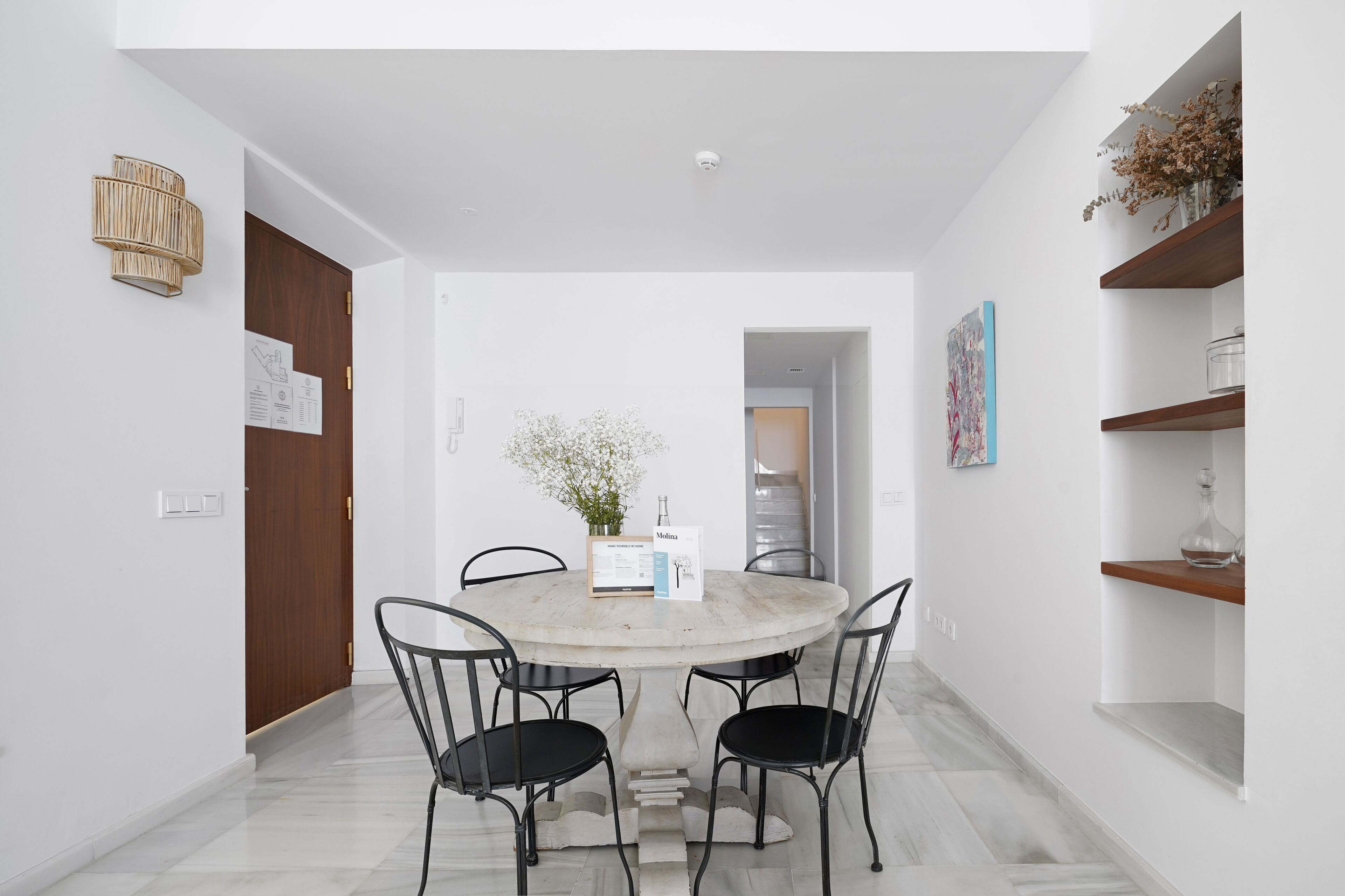 Uma área de jantar moderna com uma mesa redonda, cadeiras pretas e uma parede branca com porta de madeira.