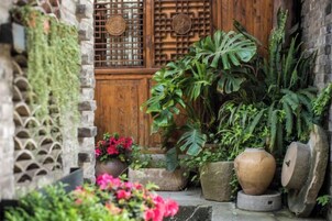 Uma porta de madeira tradicional com design em treliça, rodeada por diversos vasos de plantas e uma parede de pedra.