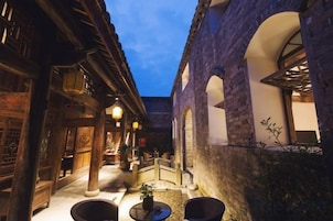 Pátio externo com arquitetura tradicional, incluindo vigas de madeira e paredes de tijolo, e área de estar com cadeiras e uma mesa.