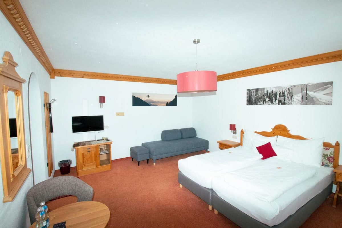 Quarto de hotel com cama, sofá, televisão, armário de madeira e espelho.
