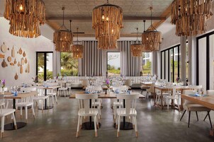 Uma sala de jantar com cadeiras brancas, mesas com peças de vidro e lustres de madeira pendentes.