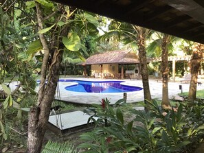Uma piscina rodeada por vegetação exuberante, com uma área de estar coberta ao fundo.