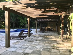 Área externa coberta com piscina, espreguiçadeiras e mesas.