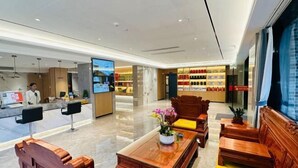 Um saguão de hotel com mobiliário de madeira, um balcão de recepção e uma tela grande.