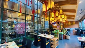 Restaurante com paredes de vidro, móveis de madeira e lanternas penduradas.