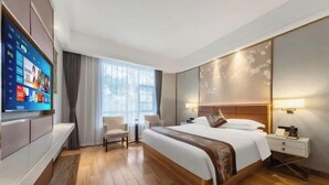 Quarto de hotel moderno com uma cama grande, televisão na parede, mesa com luminária e vista para o exterior pela janela.