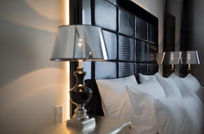 Quarto de hotel com cama, almofadas brancas, cabeceira com padrão texturizado e duas luminárias de cabeceira.