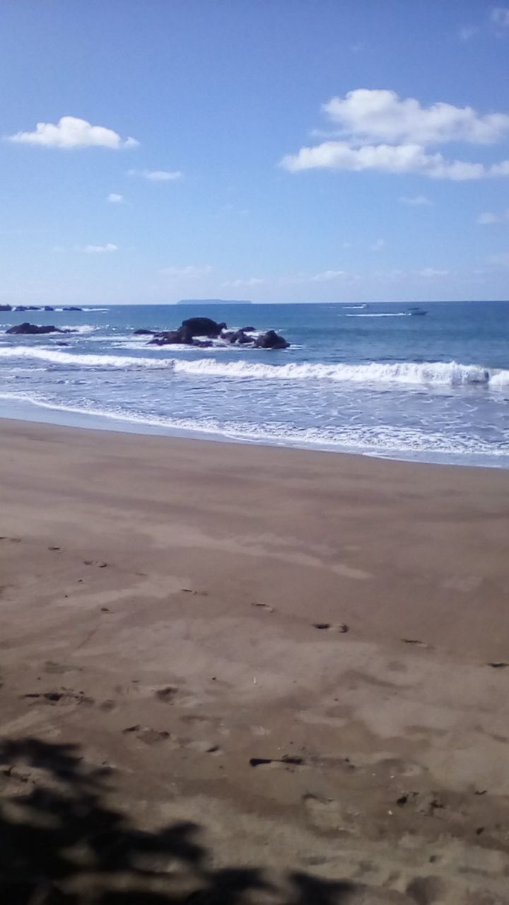 Uma praia com ondas e rochas ao longe.