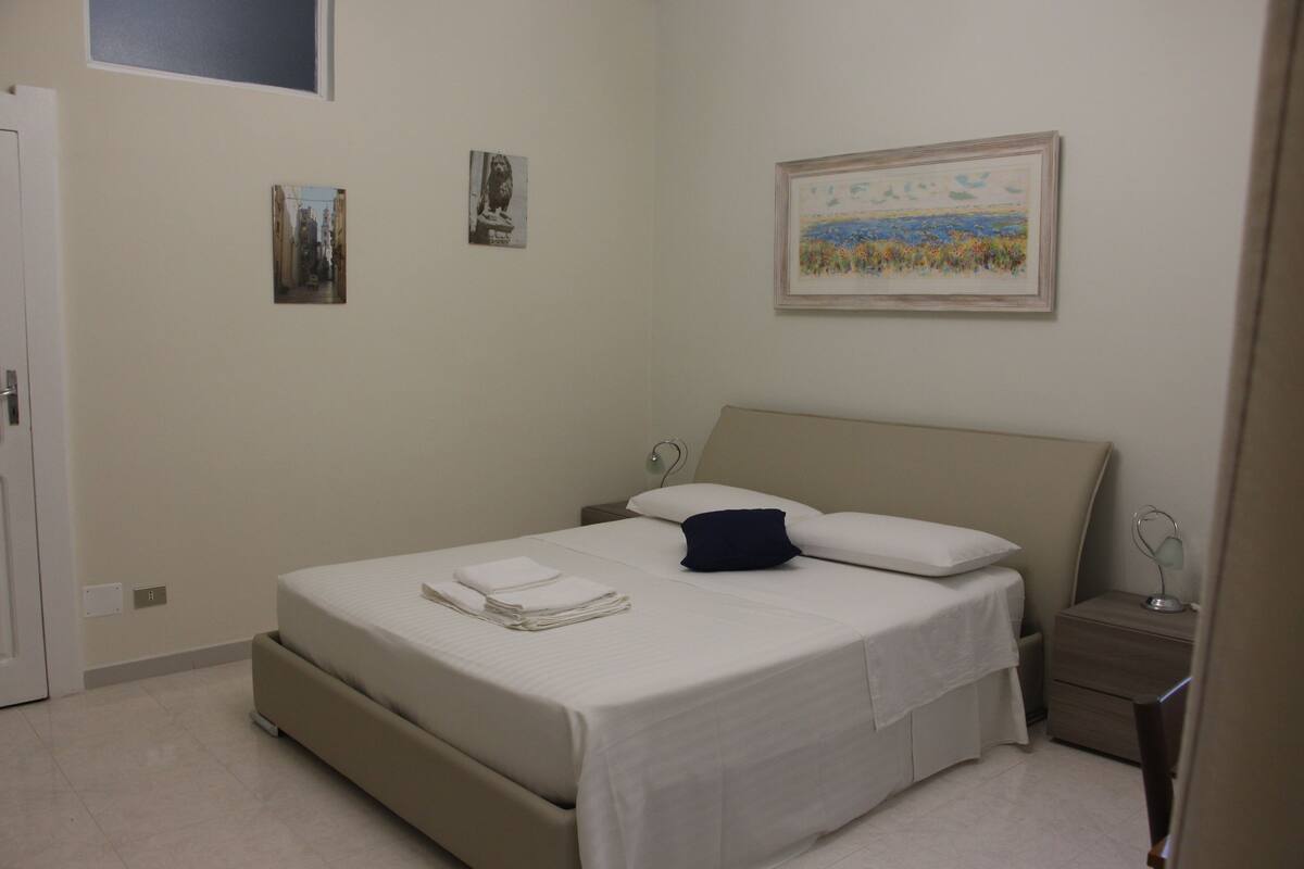 Quarto bem organizado com cama, mesas de cabeceira e obras de arte nas paredes.