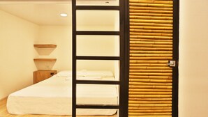 Quarto com cama, mesa de cabeceira de madeira, prateleira na parede e porta corrediça com painéis de bambu.