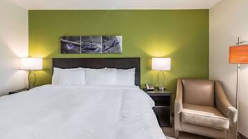 Quarto de hotel com uma cama grande, duas mesas de cabeceira com luminárias, uma cadeira e uma parede verde decorada com obras de arte.