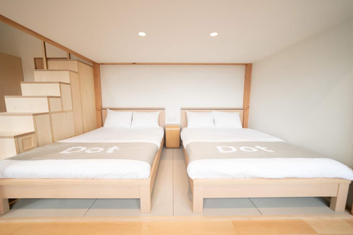 Quarto de hotel moderno com duas camas de madeira, uma escada e uma janela grande.