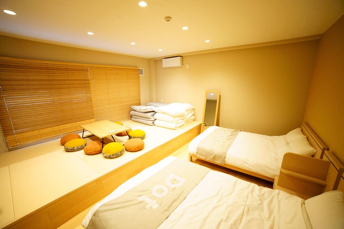Quarto de hotel com duas camas, uma mesinha, um espelho e uma janela com persianas.