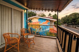Uma varanda com cadeiras de vime, uma mesa de vidro e um mural colorido com tema tropical.
