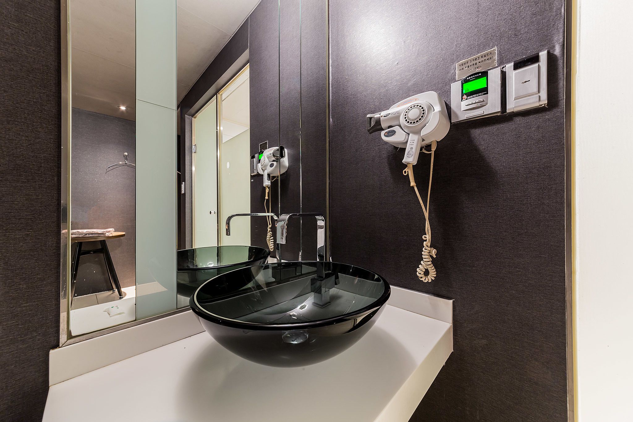 Casa de banho moderna com lavatório de vidro preto, secador de cabelo portátil e espelho.