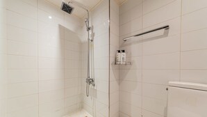 Uma casa de banho moderna com cabine de duche em vidro, sanita e prateleira com artigos de higiene pessoal.