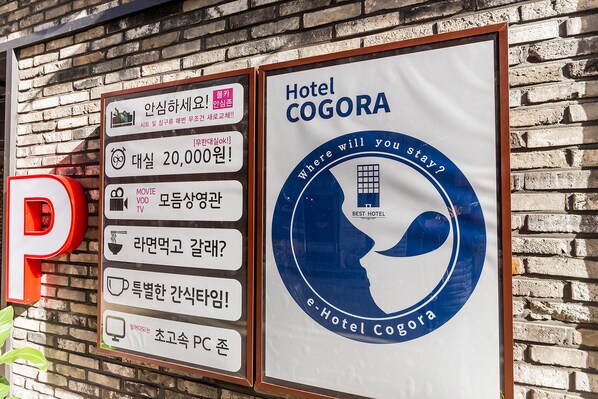 Placa do Hotel Cogora com comodidades listadas em coreano, incluindo preço de 20.000 won, sala de cinema e TV e sala de computadores.