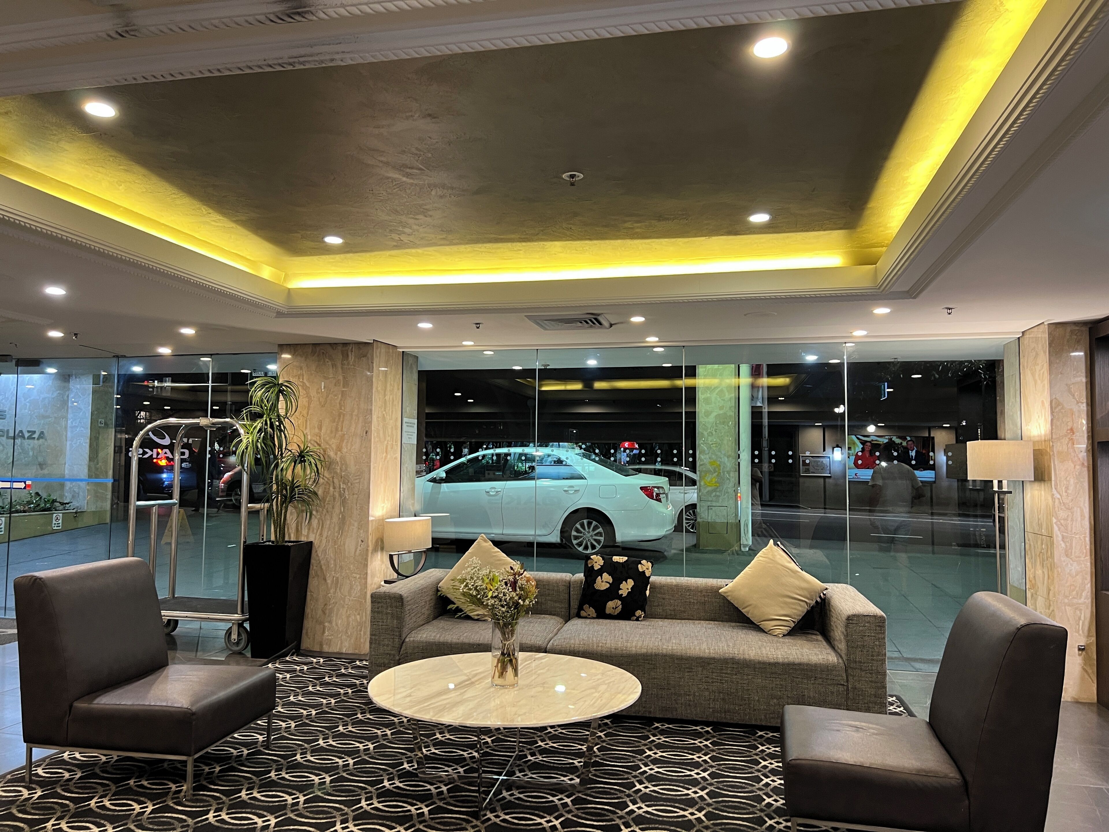 Um hall moderno com sofá, cadeiras, uma mesa de centro e um carro visível pelas portas de vidro.