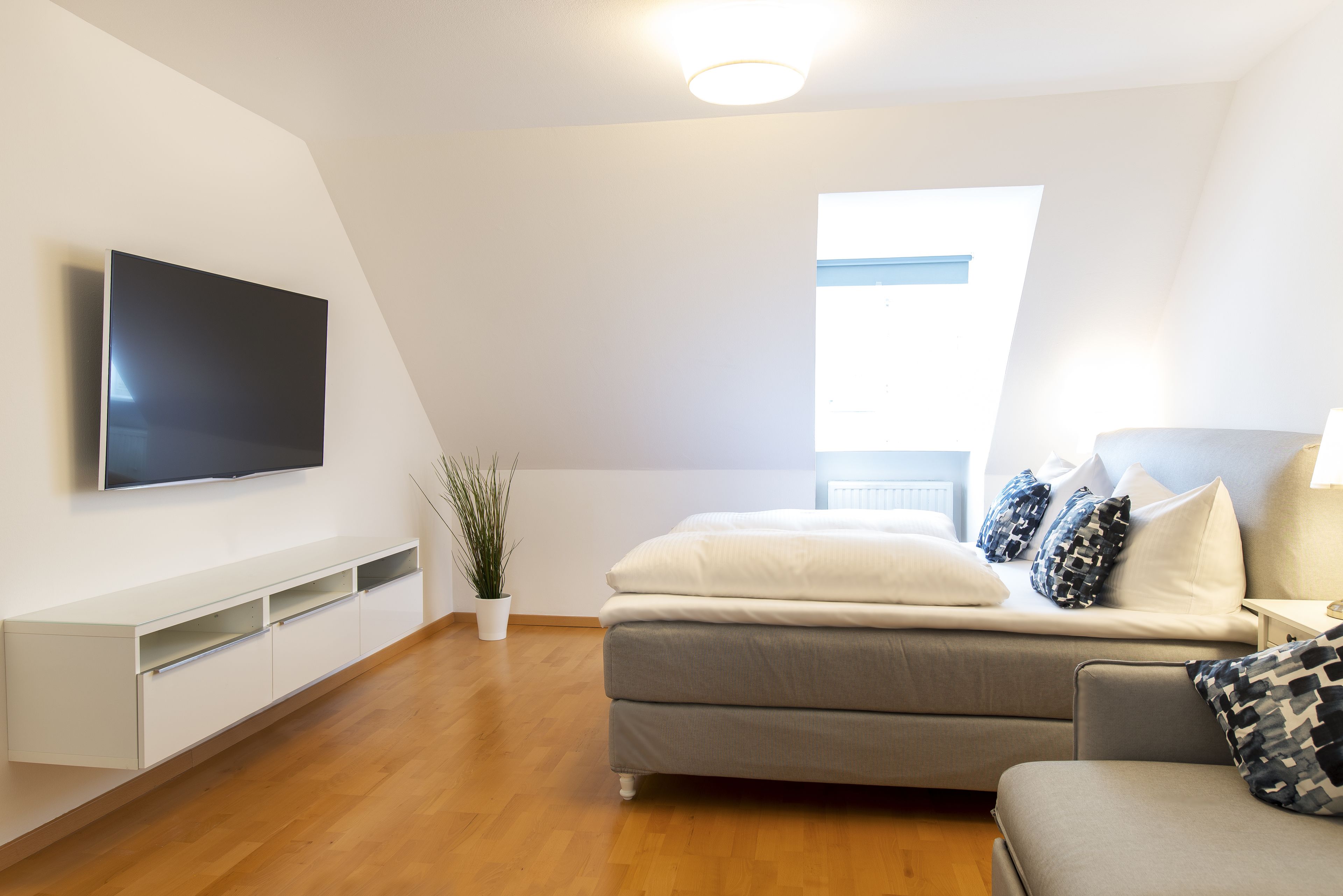 Quarto moderno com cama, TV na parede e janela que traz luz natural.
