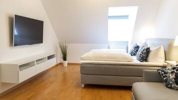 Quarto moderno com cama, TV na parede e janela que traz luz natural.