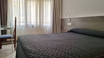 Quarto de hotel com uma cama, uma escrivaninha e uma cadeira.