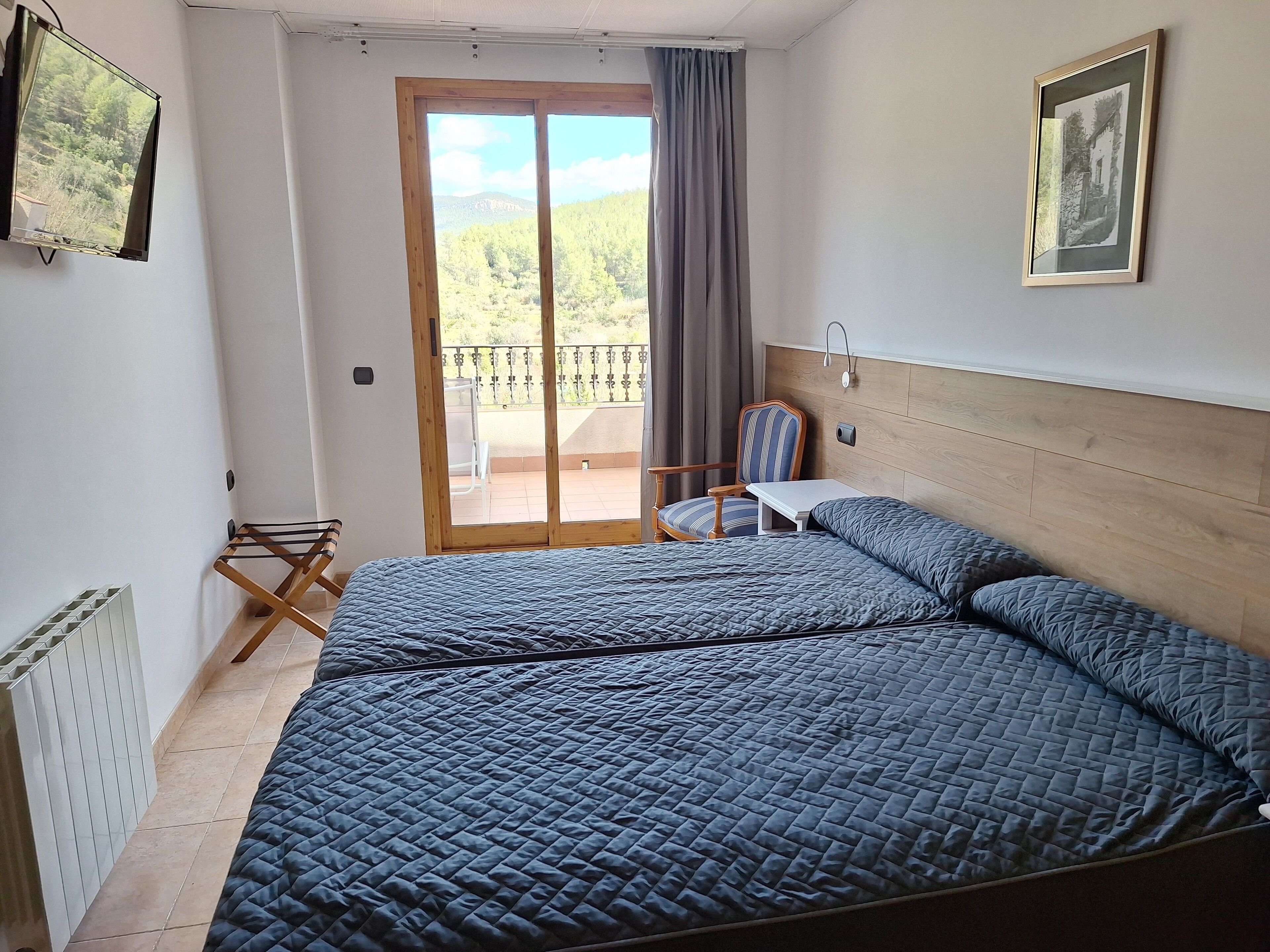 Quarto com uma cama grande, uma cadeira, uma mesinha e vista para uma varanda com guarda-corpo.