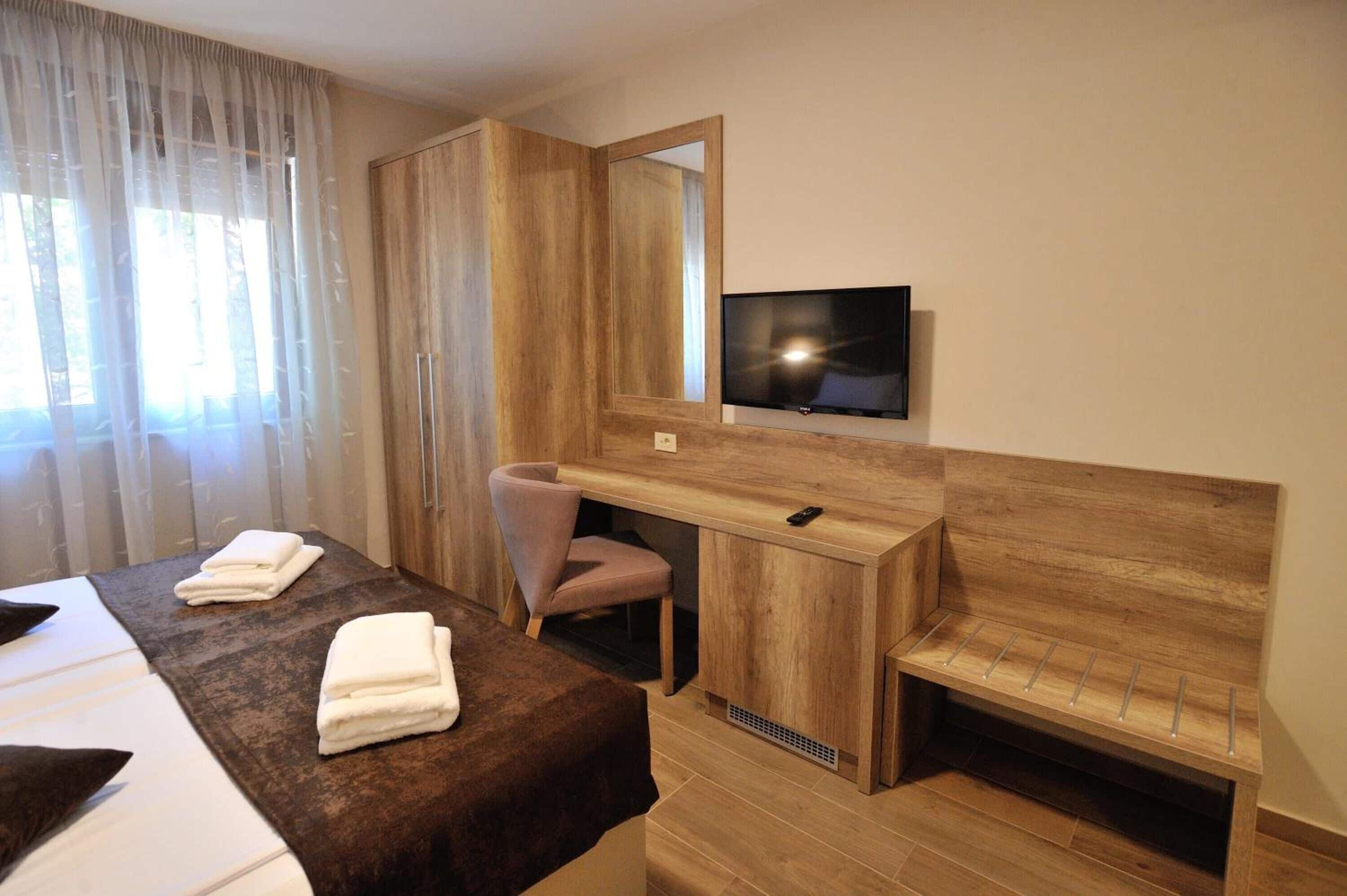 Quarto de hotel com uma cama, uma escrivaninha com cadeira, televisão e um espelho grande.