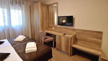 Quarto de hotel com uma cama, uma escrivaninha com cadeira, televisão e um espelho grande.