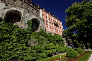 Um edifício histórico com estruturas em arco e fachada vermelha, rodeado por vegetação exuberante.